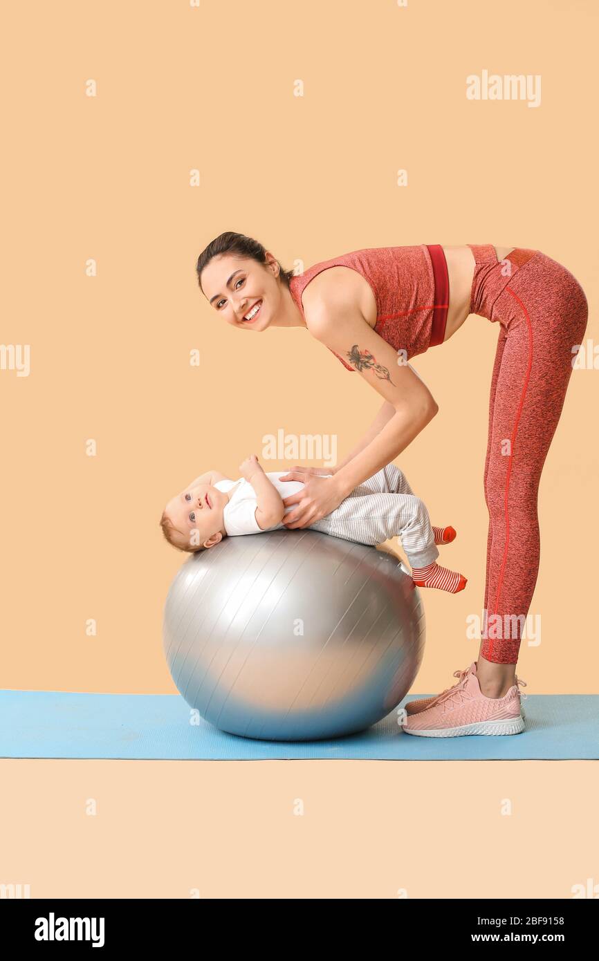 Young sporty mother and her baby doing exercises with fitball on color background Stock Photo ...