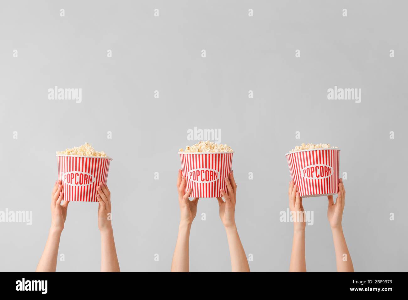 Many hands with popcorn in buckets on grey background Stock Photo - Alamy