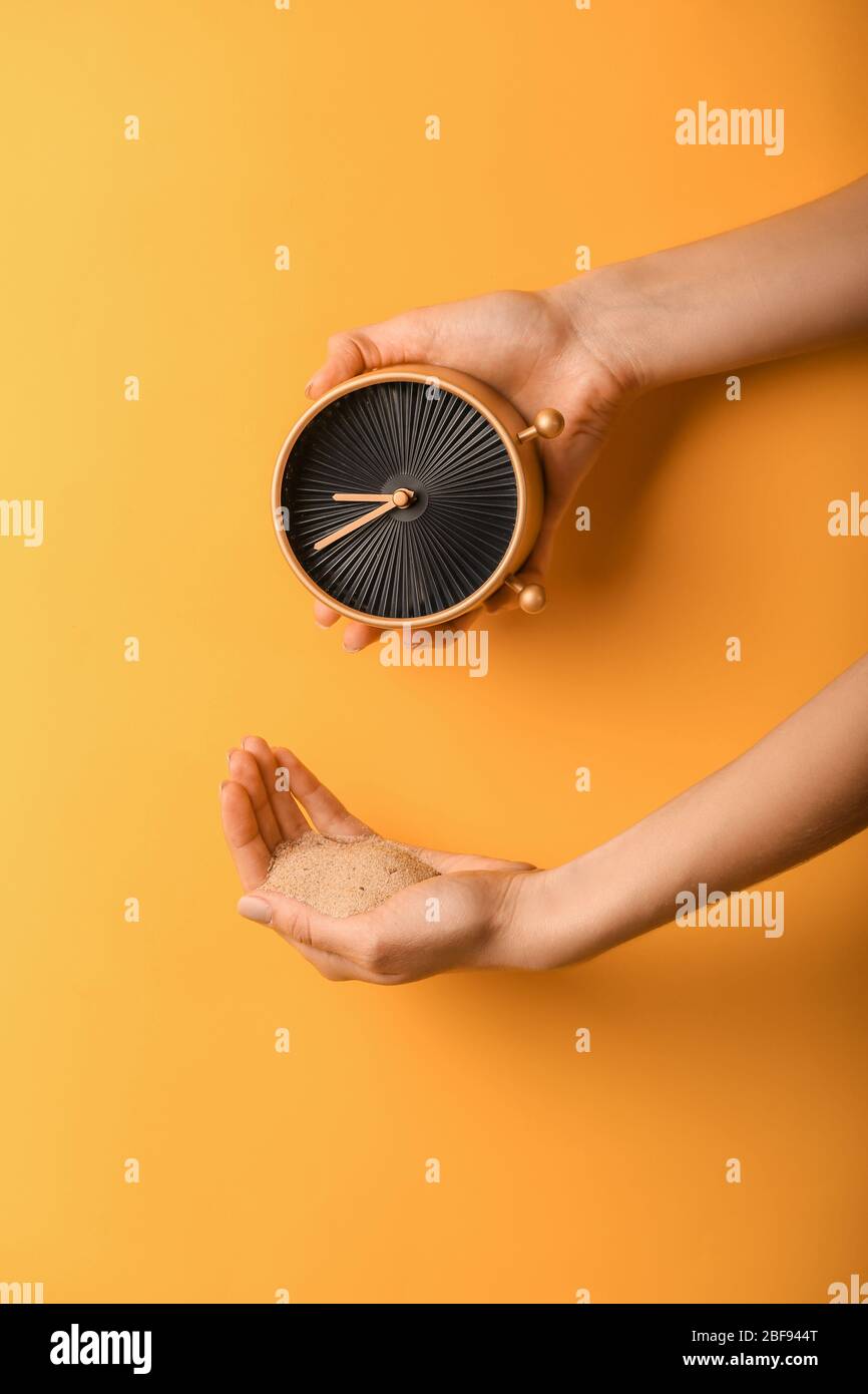 Female hands with clock and sand on color background. Time management ...