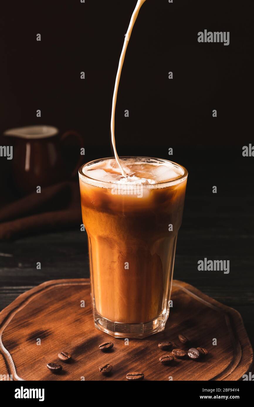 Pouring of milk into cold coffee in glass on table Stock Photo - Alamy