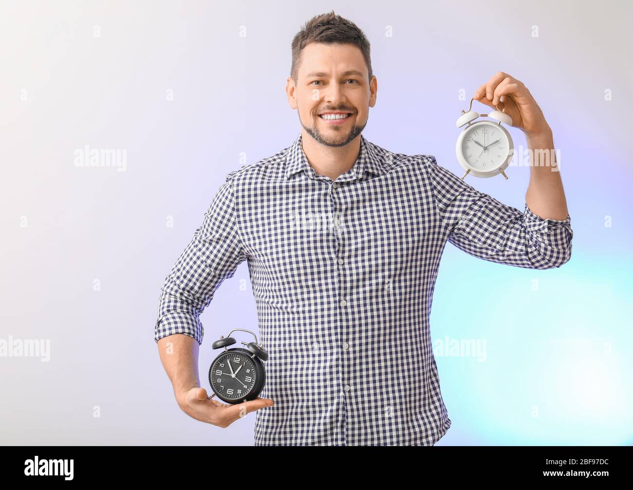 Man with alarm clocks on light background. Time management concept ...