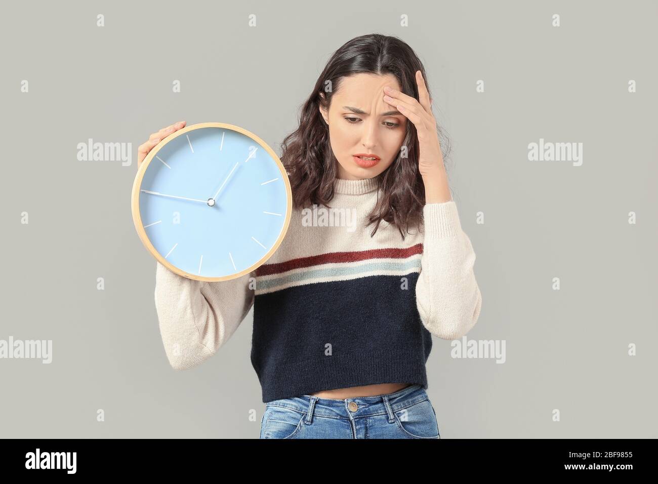 Worried woman with clock on grey background. Time management concept ...
