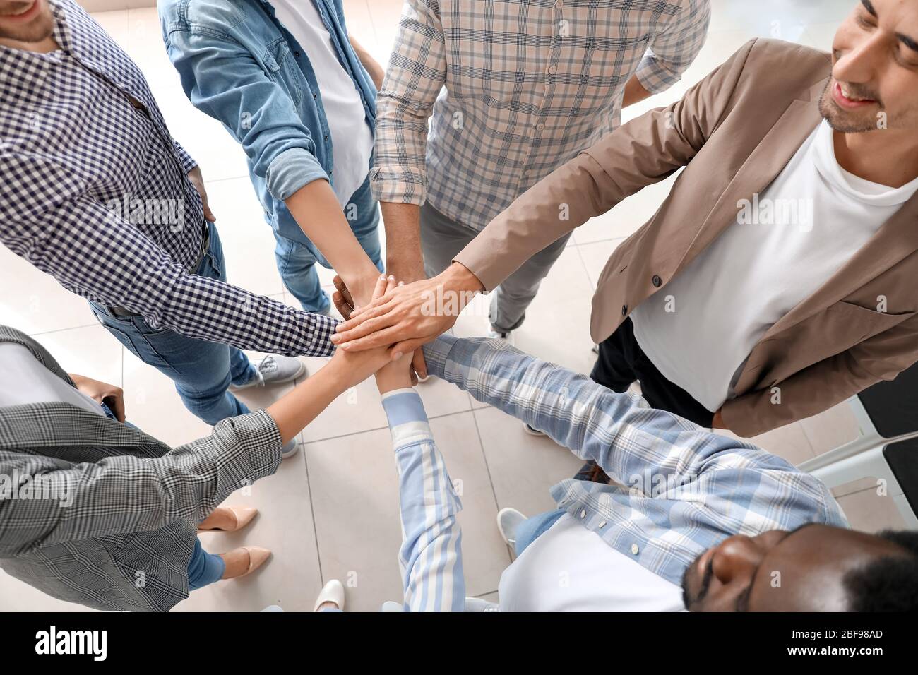 Group of people putting hands together indoors, top view. Unity concept ...