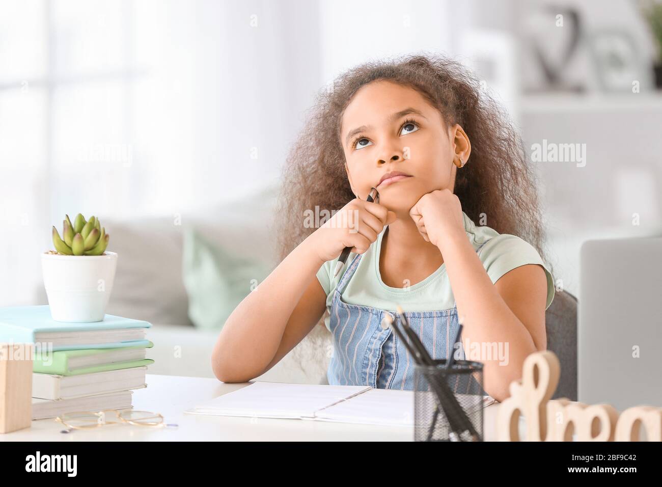 Thoughtful African-American girl doing homework in room Stock Photo - Alamy