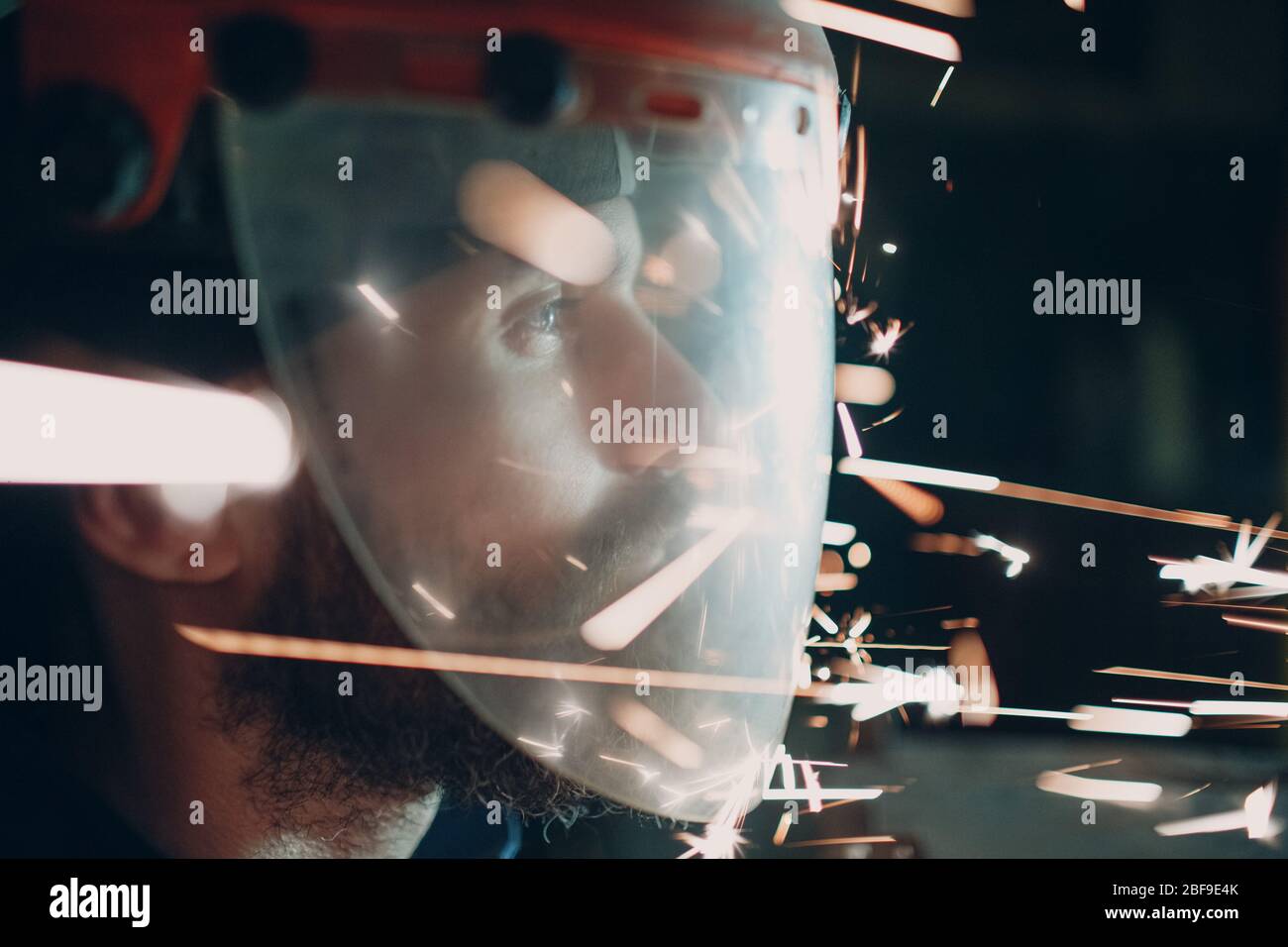 Adult bearded man in transparent protective mask with flying metal ...