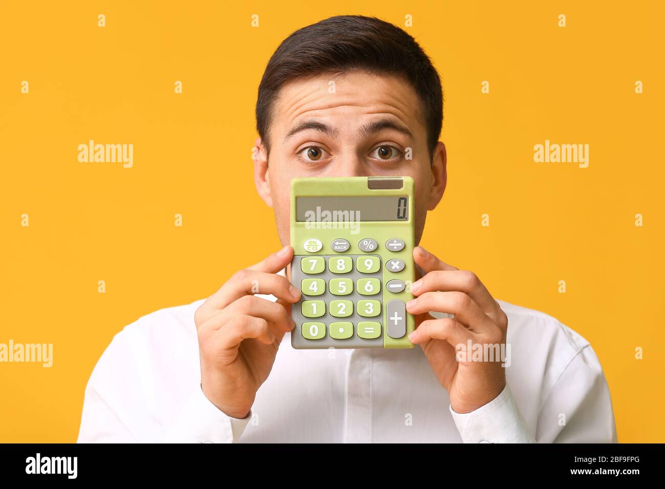 Surprised young man with calculator on color background Stock Photo - Alamy