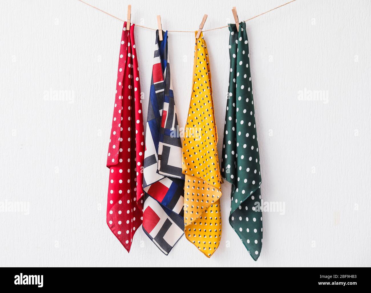 Different beautiful scarves hanging on rope against white background ...