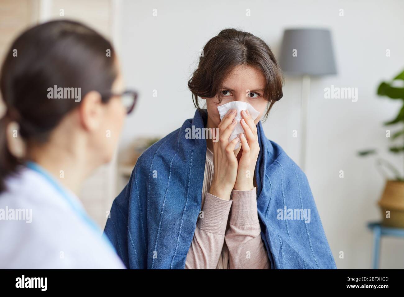 Sick young woman sitting with doctor and talking to her about the ...
