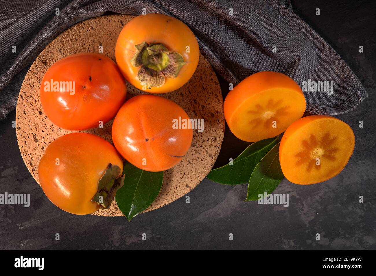 Ripe persimmon fruits in a cork plate on dark kitchen counter top Stock ...