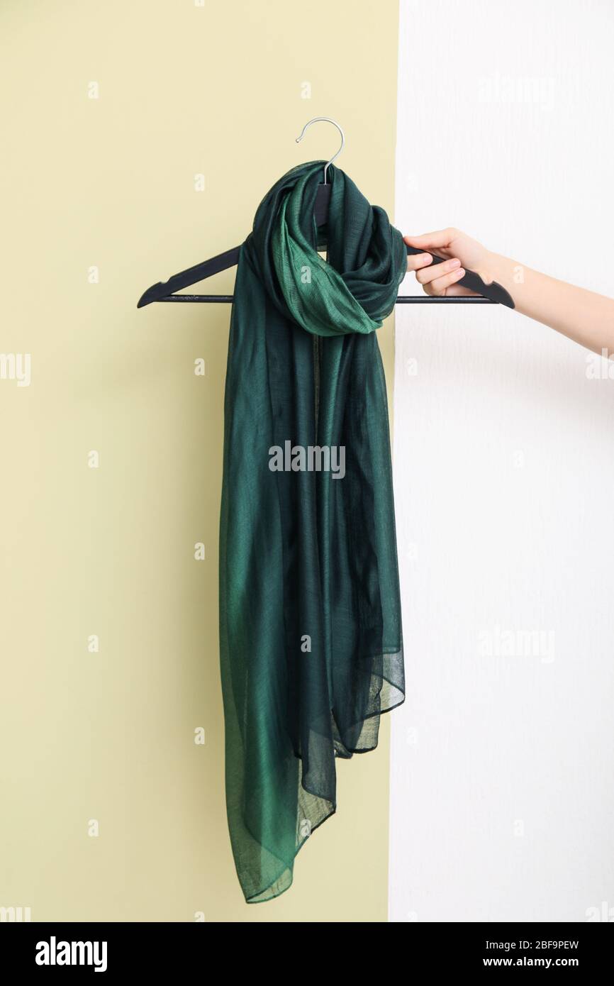 Female hand holding hanger with beautiful scarf on light background ...