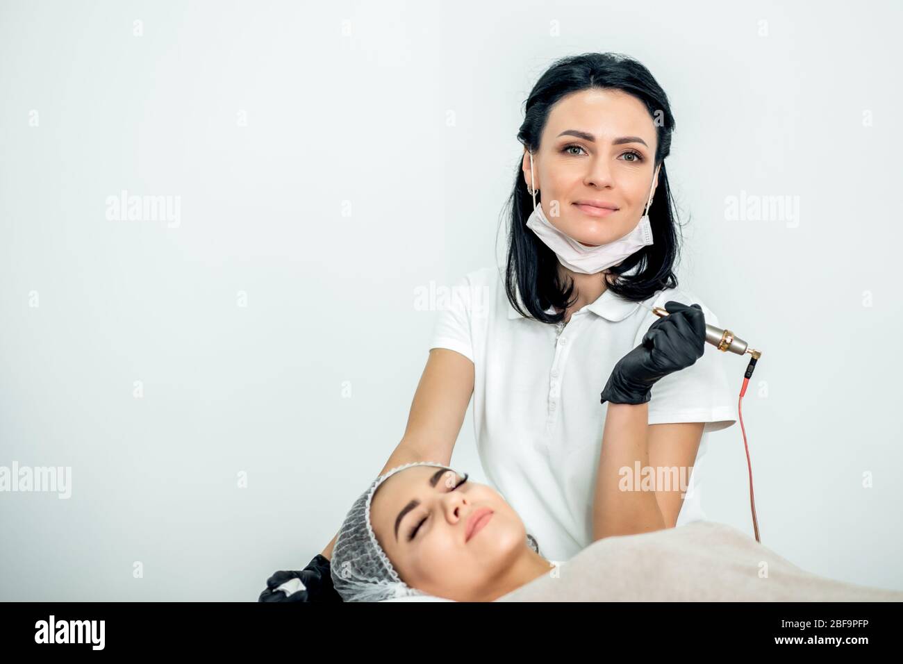 Cosmetologist with patient during eyelash extension procedure standing ...