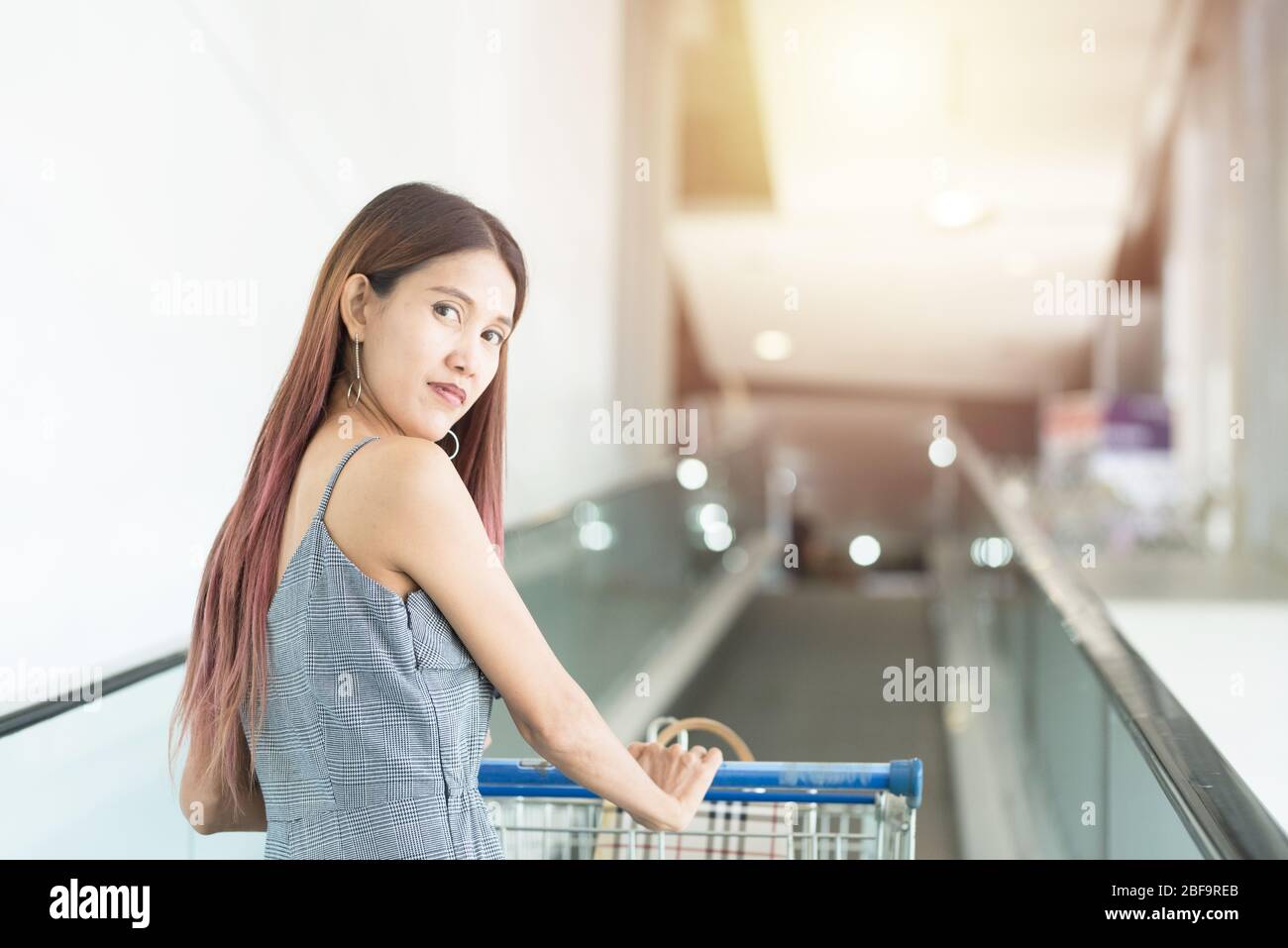 Asian shopper woman with shopping cart on moving walkway up to second ...