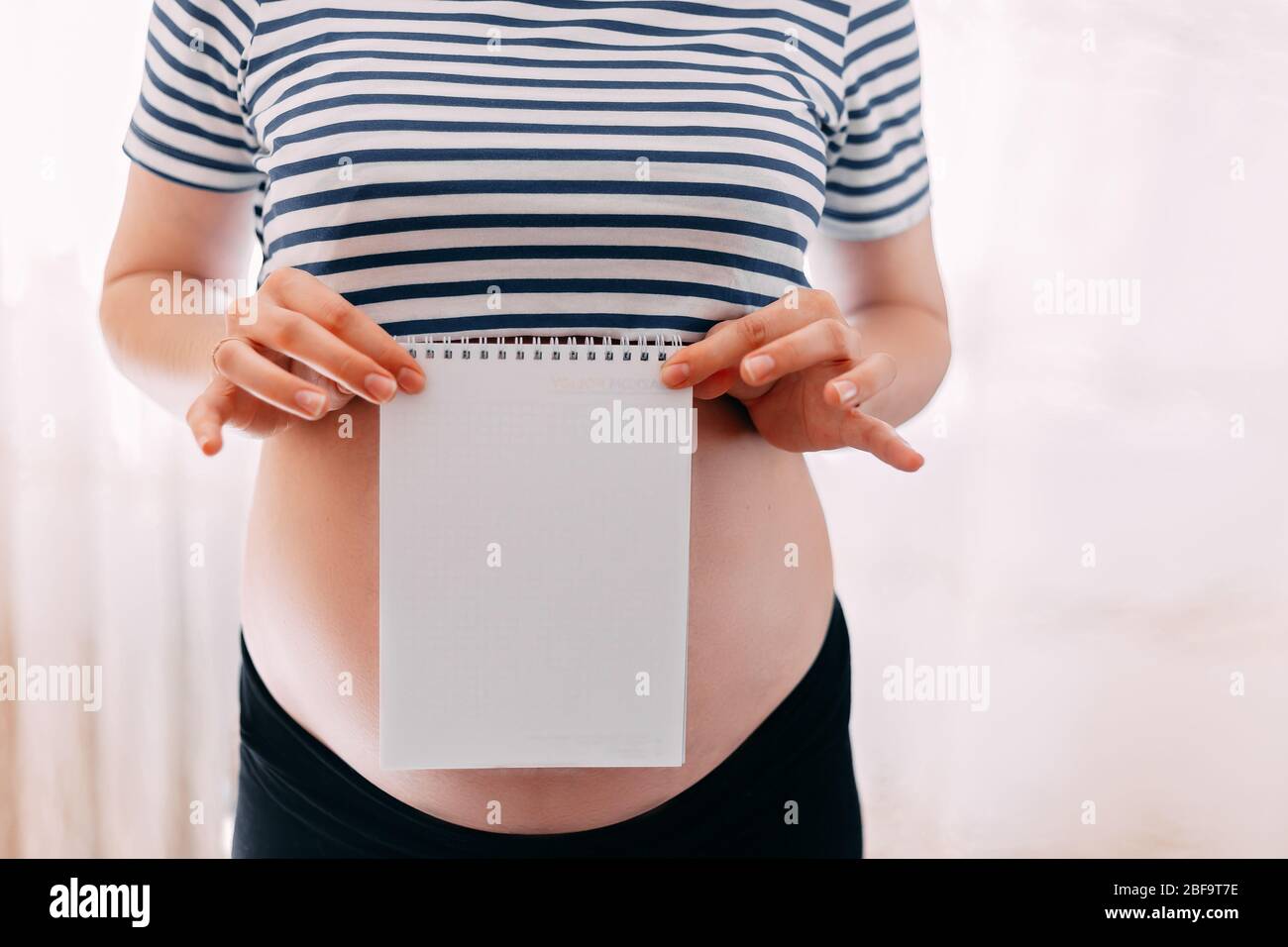 Cheerful pregnant woman making notes in jotter, focuse on paper, belly ...