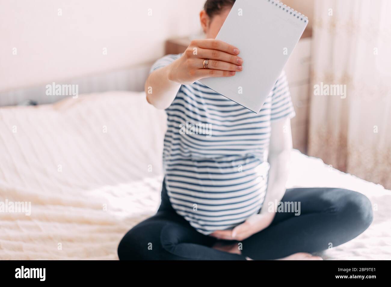 Cheerful pregnant woman making notes in jotter, focuse on paper, belly ...