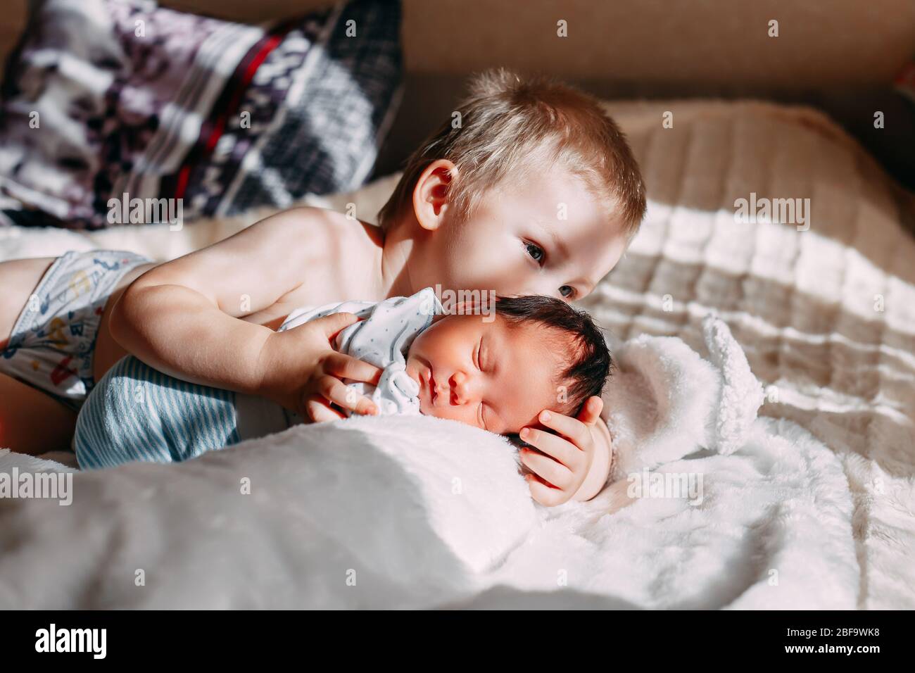 Happy little brother with newborn baby lying in a bed together, kissing ...