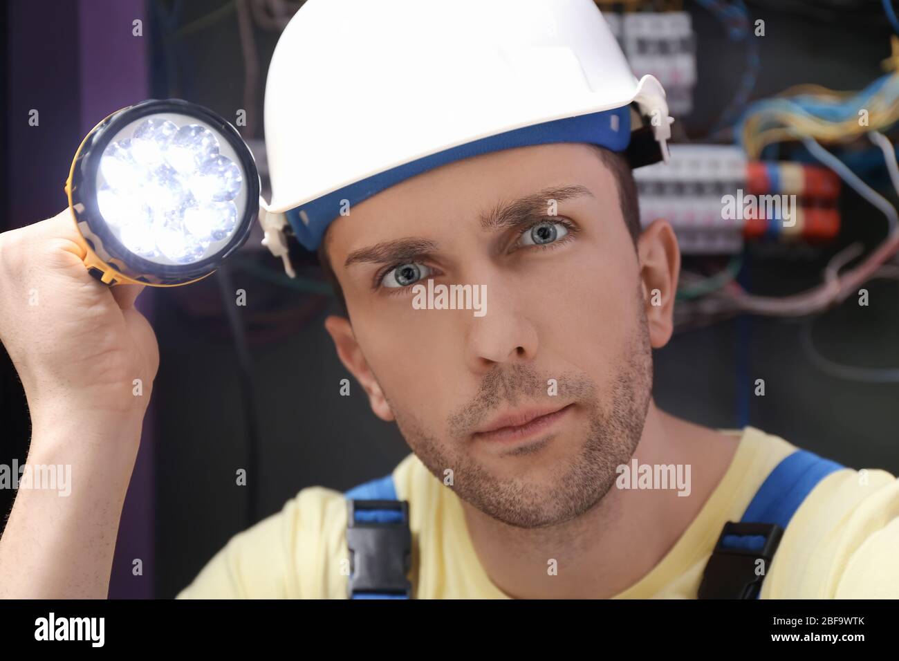 Male electrician with flashlight repairing distribution board Stock ...
