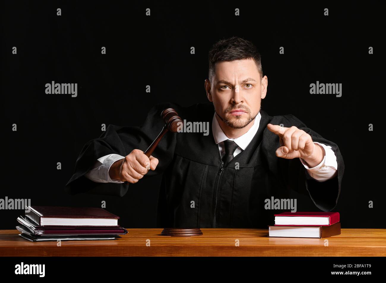 Strict male judge at table on dark background Stock Photo - Alamy