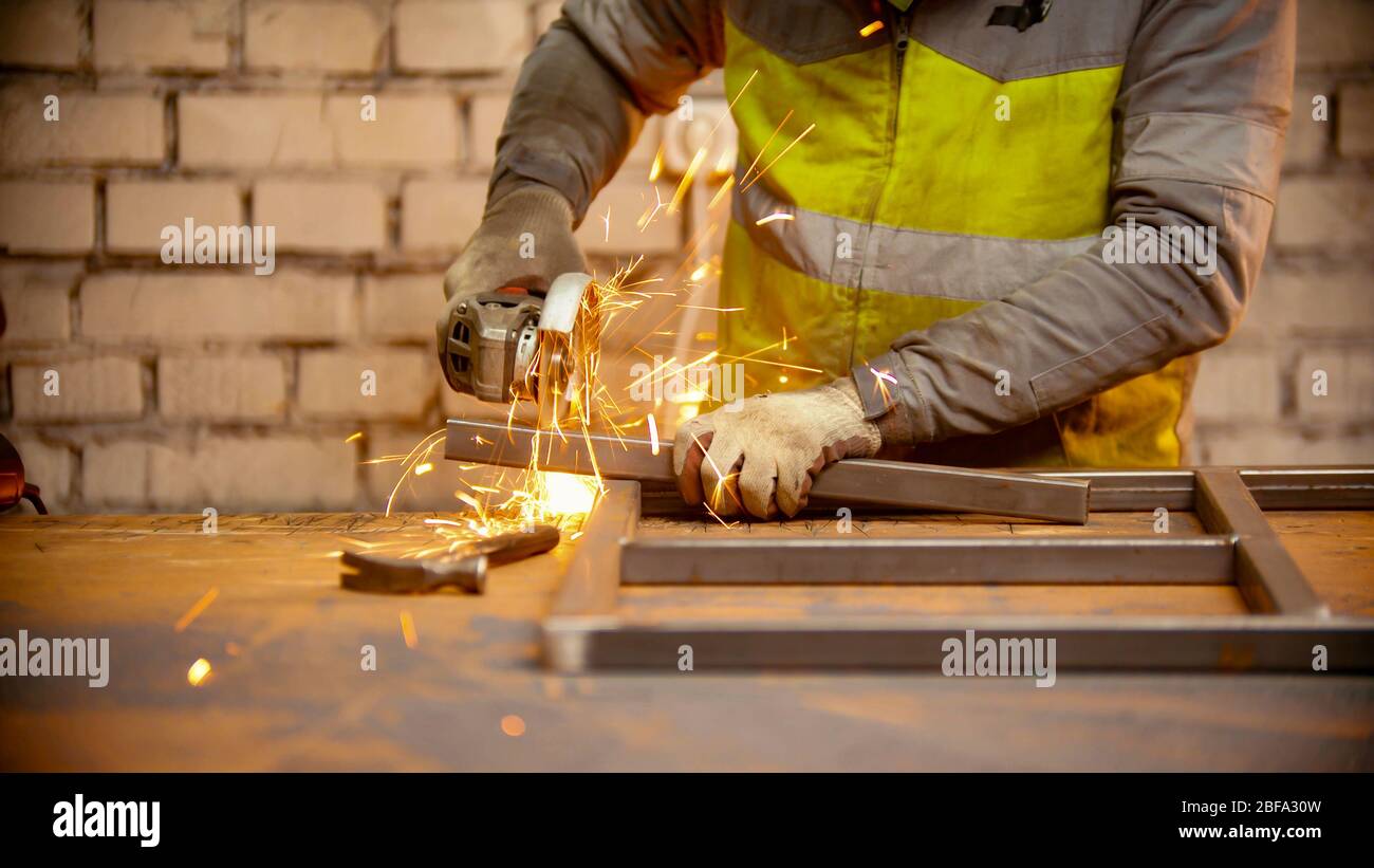 A man worker cutting the metal beam using grinder machine. Mid shot ...