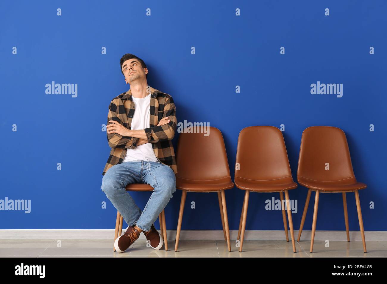 Waiting young man sitting on chair near color wall Stock Photo - Alamy