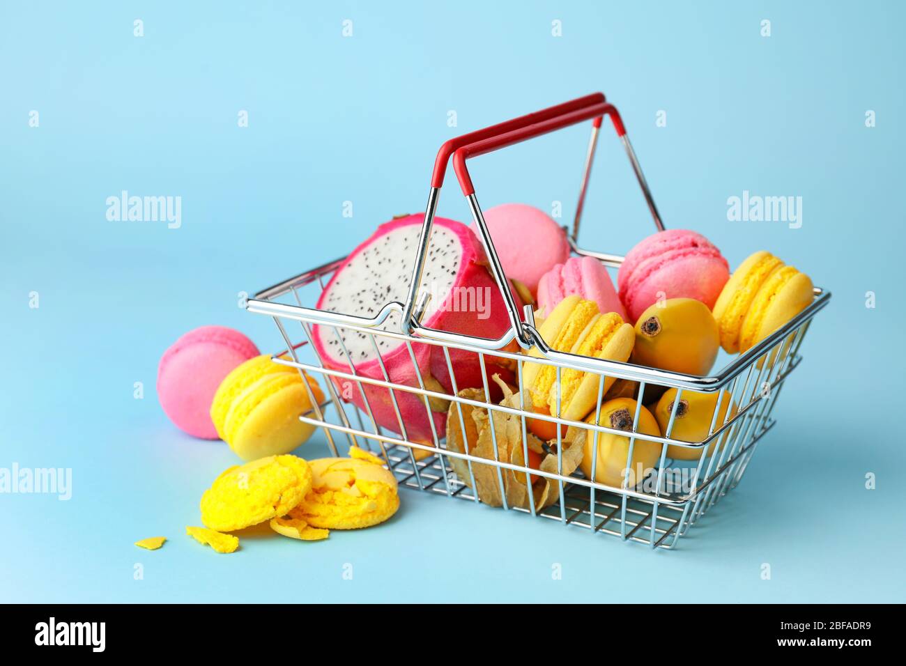 Tasty macarons with fruits in shopping basket on color background Stock ...