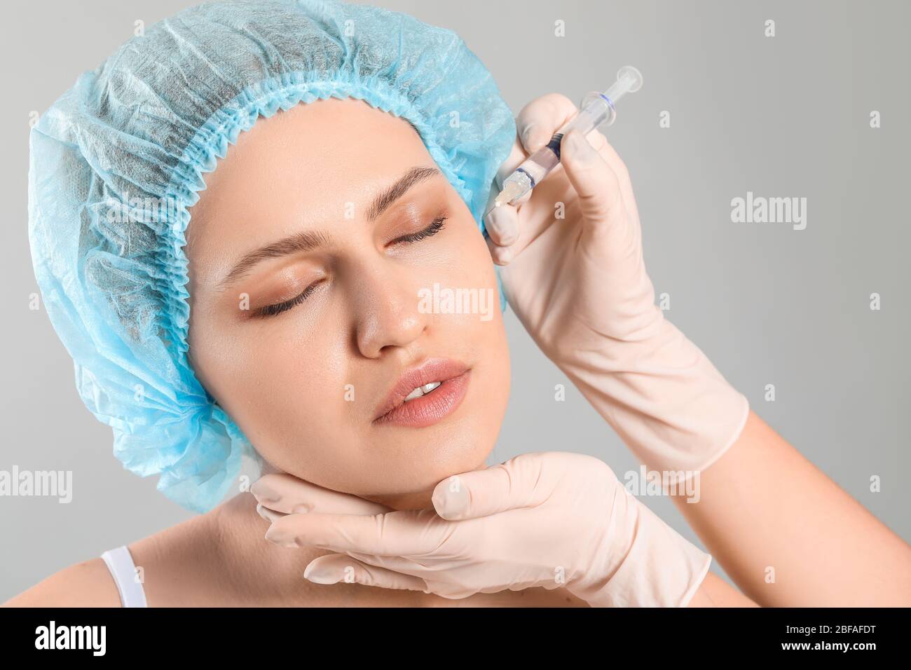Young woman receiving filler injection on grey background Stock Photo ...