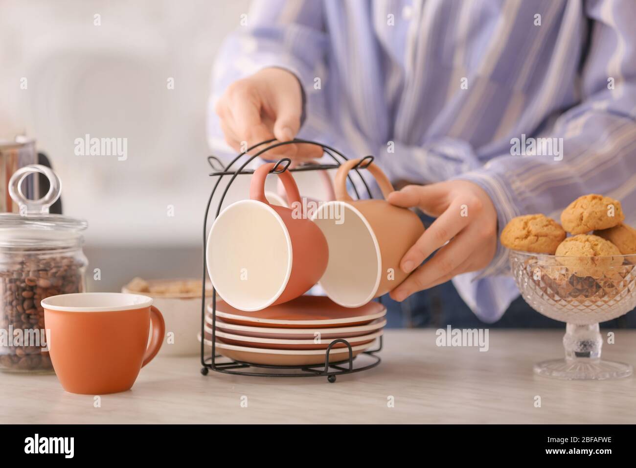 Woman taking holder for cups and saucers from kitchen table Stock Photo ...