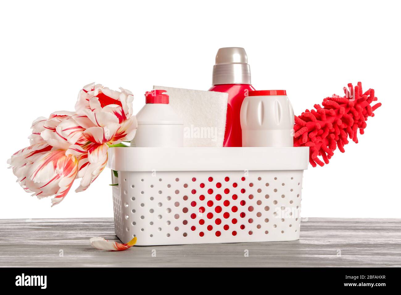 Set of cleaning supplies and spring flowers on table against white ...