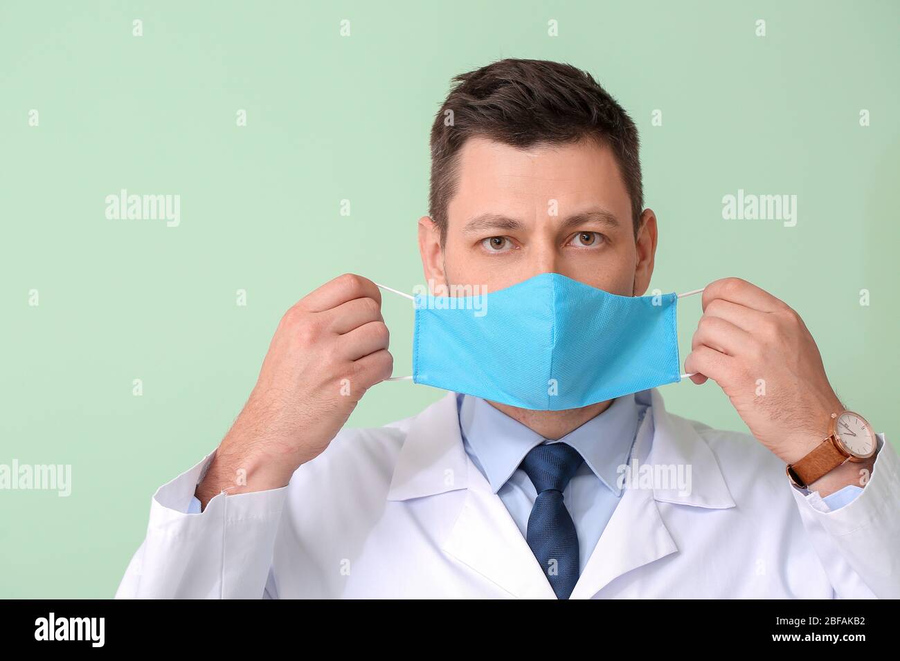 Doctor putting on protective medical mask against color background ...