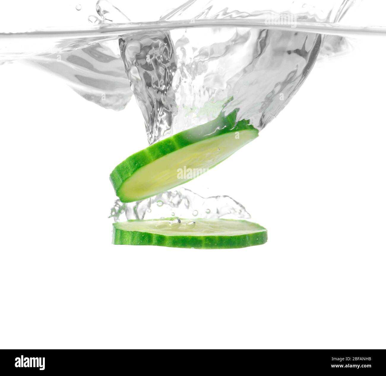 Falling of fresh cucumber slices into water against white background Stock Photo - Alamy