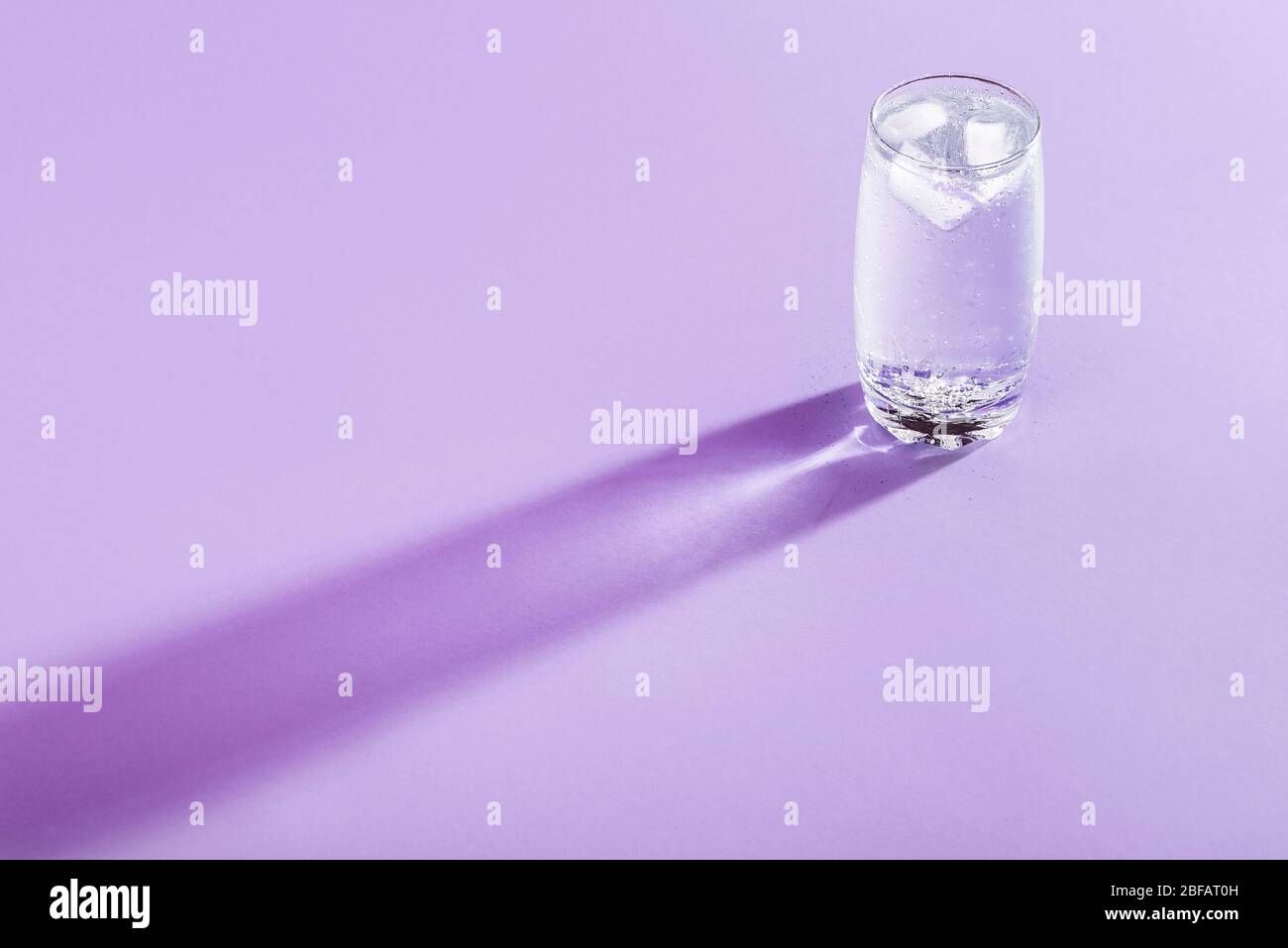 Single glass with tonic water and ice cubes on a purple background ...