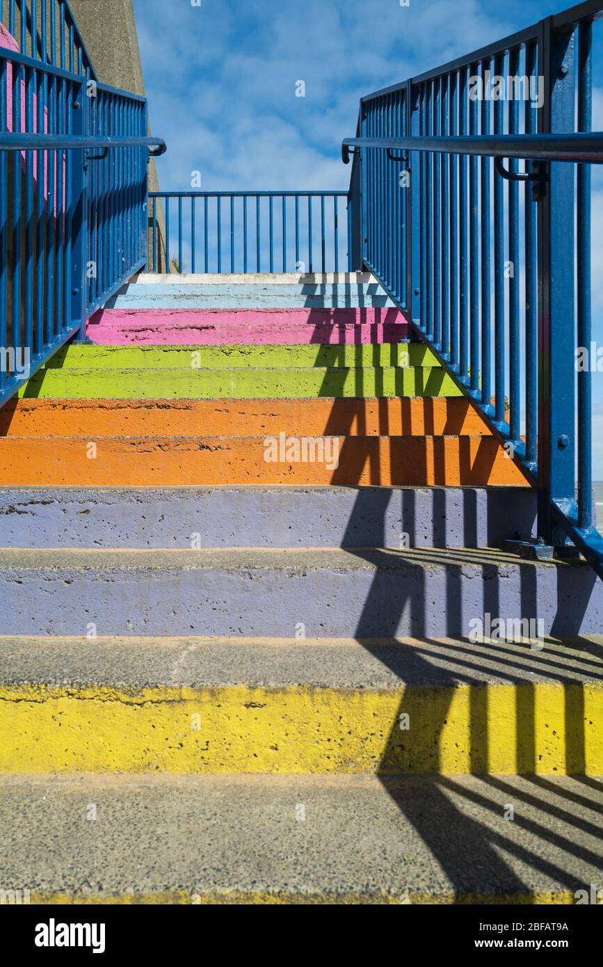 Concrete steps painted bright rainbow colours with a blue railing and a ...