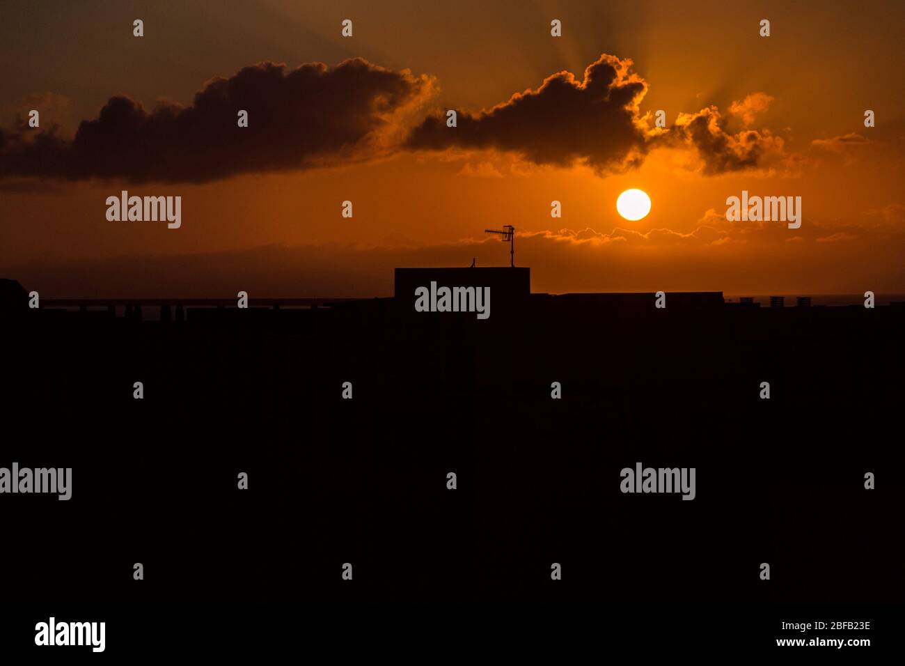 Sun rising behind roof with antenna, dramatic clouds and large black ...