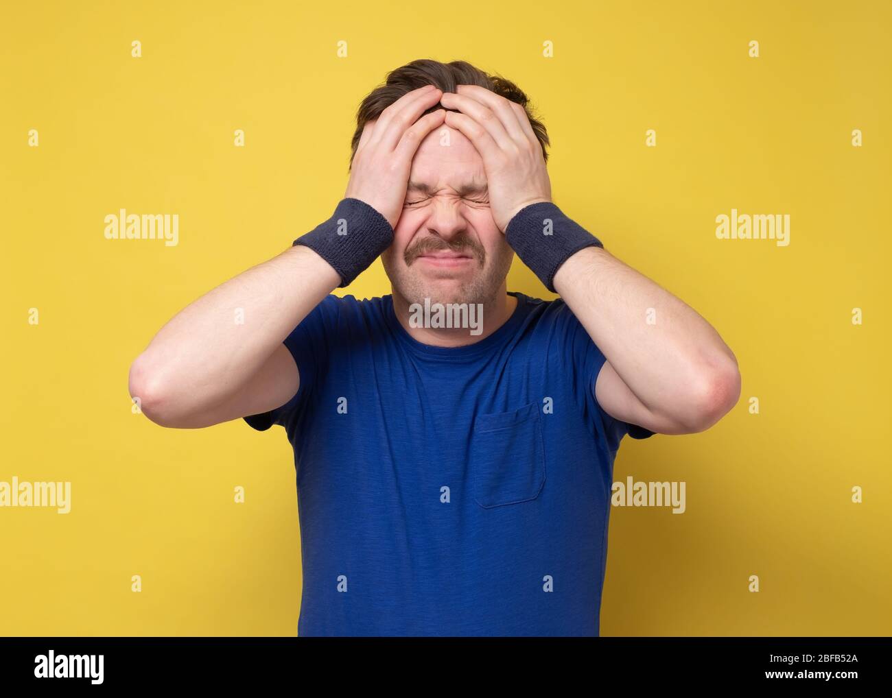Exhausted and tired young man grabs his head from fatigue and stress ...