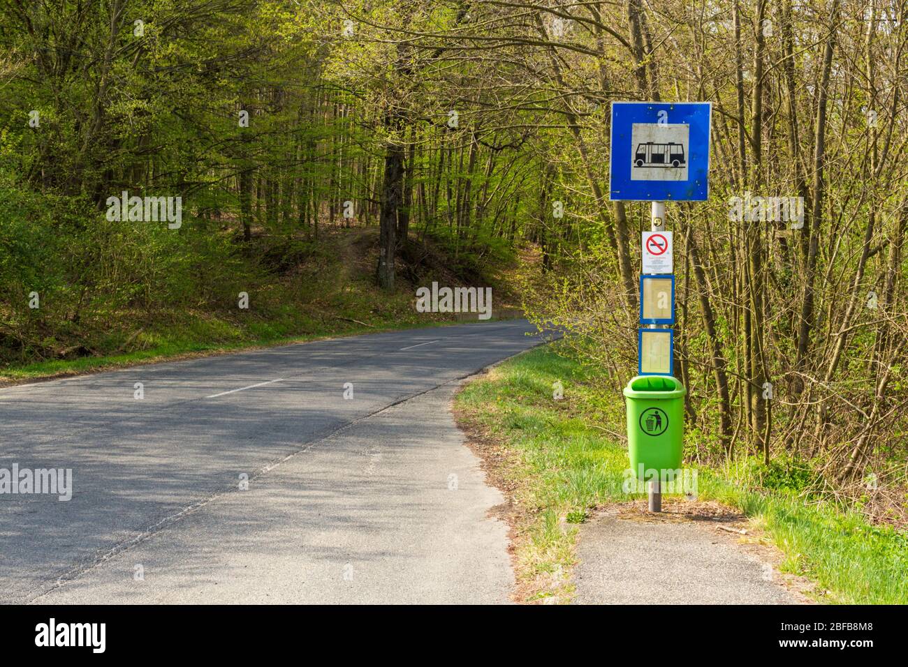 Bus stop with no smoking sign and green garbage bin beside road through ...