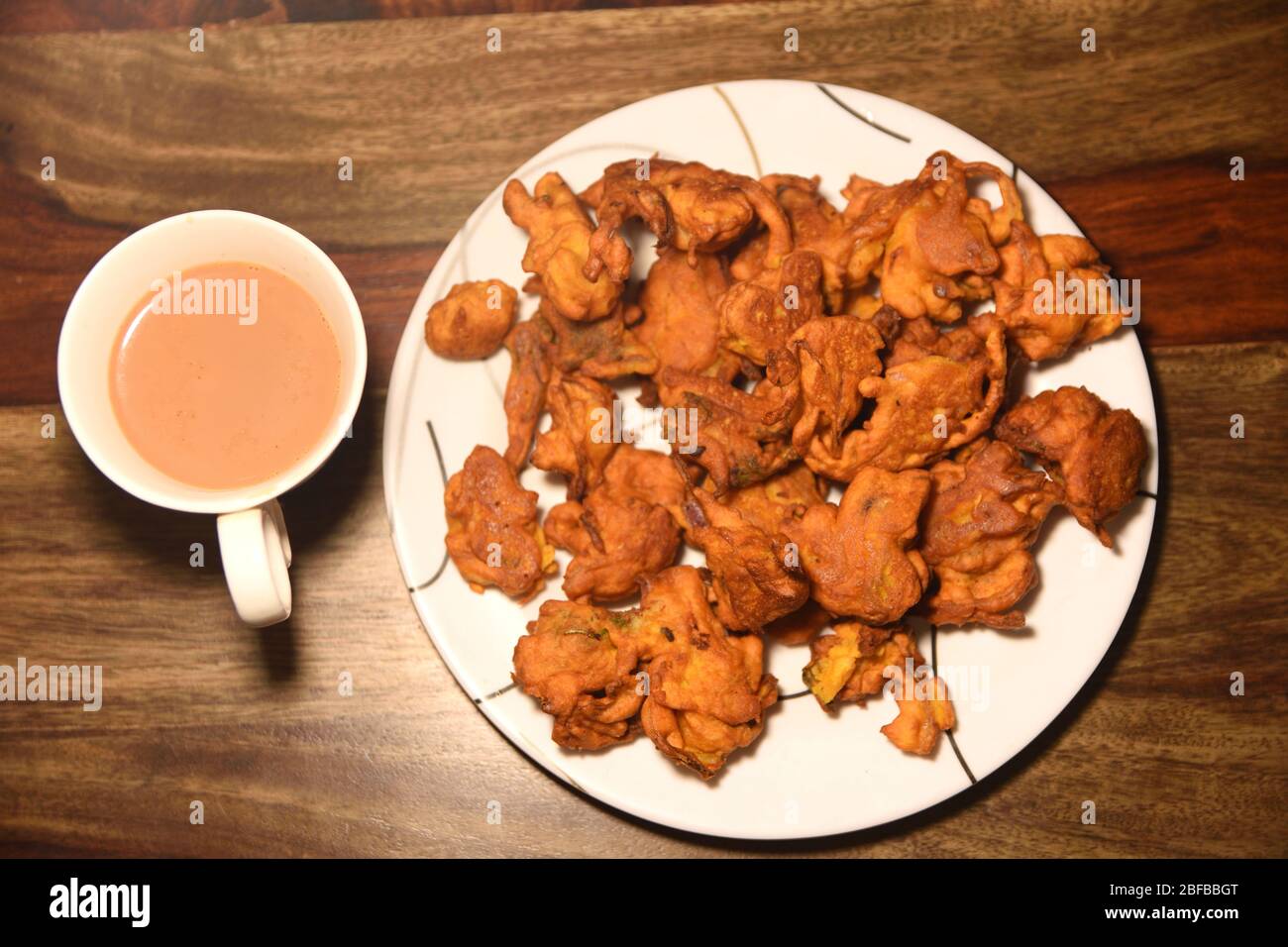Chai with pakoras and bhajiyas and served on plate on wooden background ...