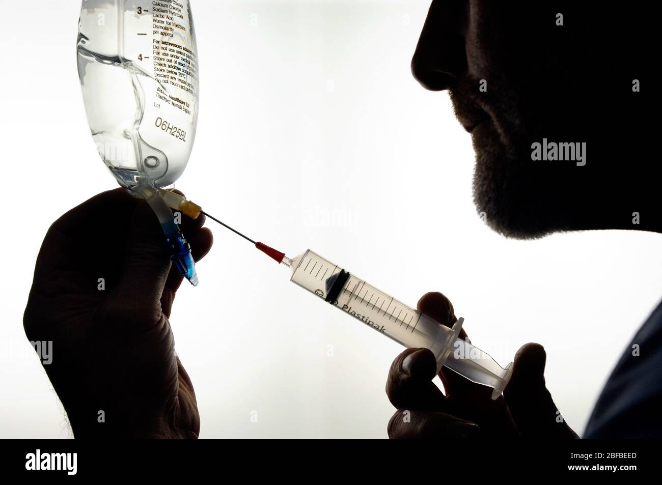 In a shadow, a doctor draws sodium lactate solution into a syringe ...