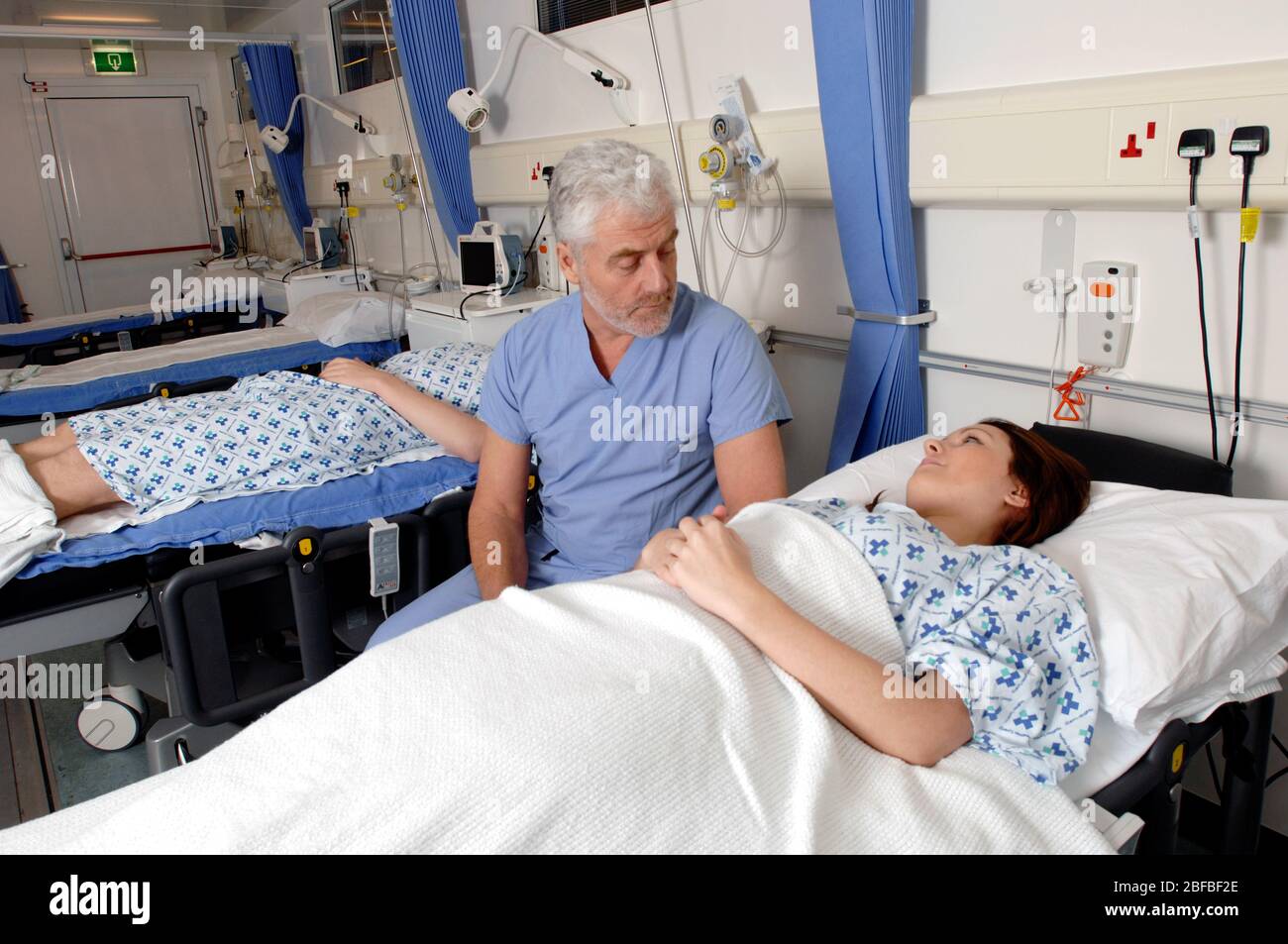 A bearded surgeon sits at the hospital bedside of a female patient ...