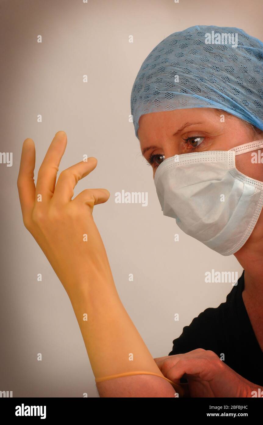 A hospital worker, wearing a hygiene mask and hygiene hat, puts on a ...