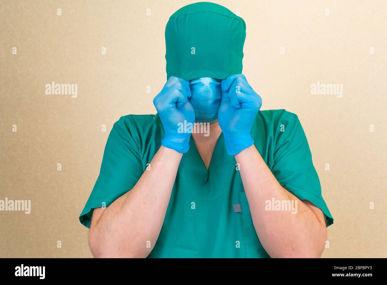 Doctor in green suit and blue gloves hiding face under mask an hat ...