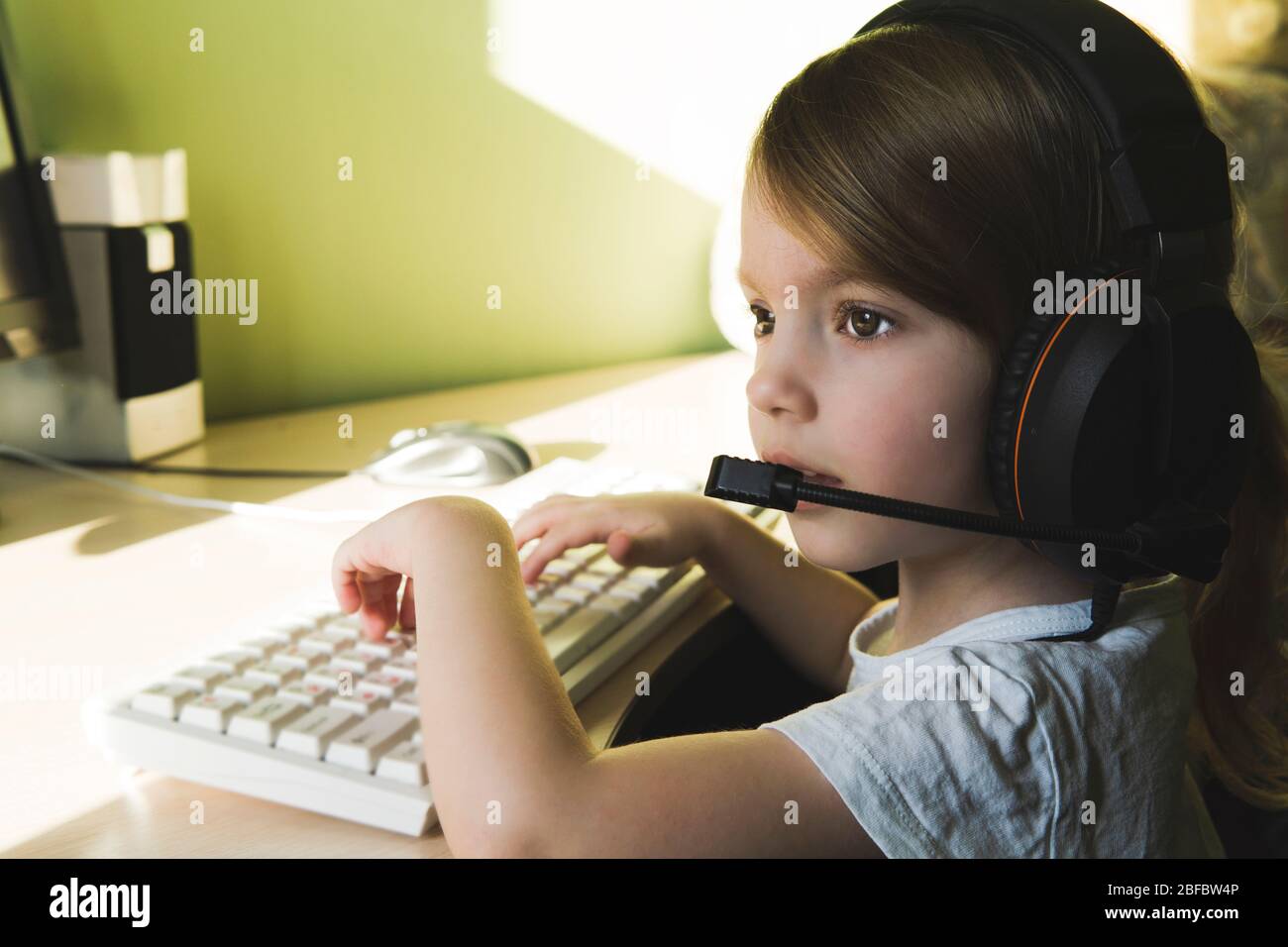 Little girl sitting at the computer with earphones on the head ...