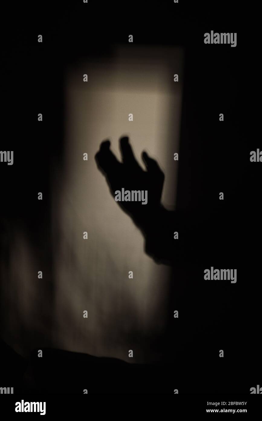The shadow of a partially clenched hand shows in the light on a dark ...