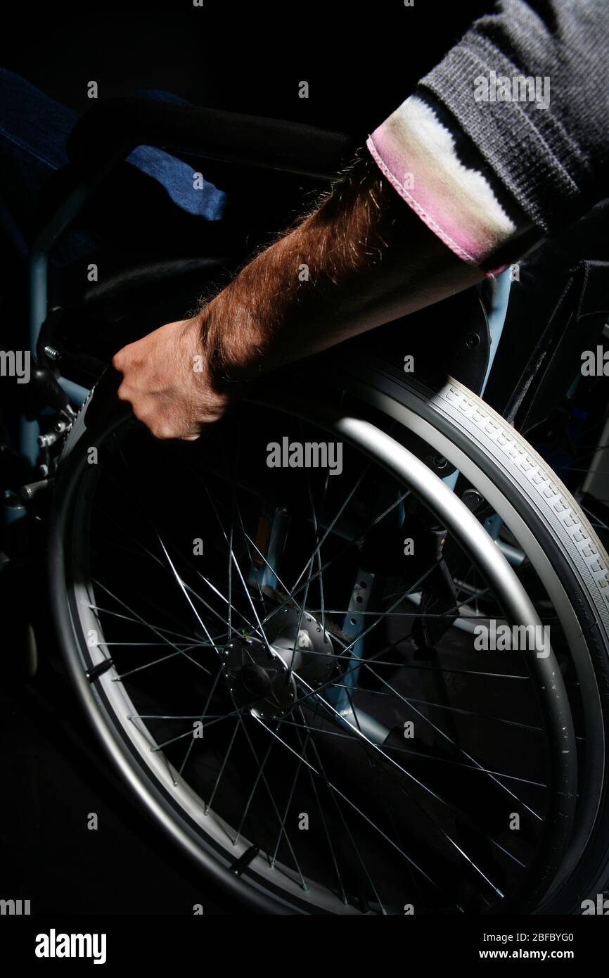 A close-up of the hand of a wheelchair user, using his hand to move his ...