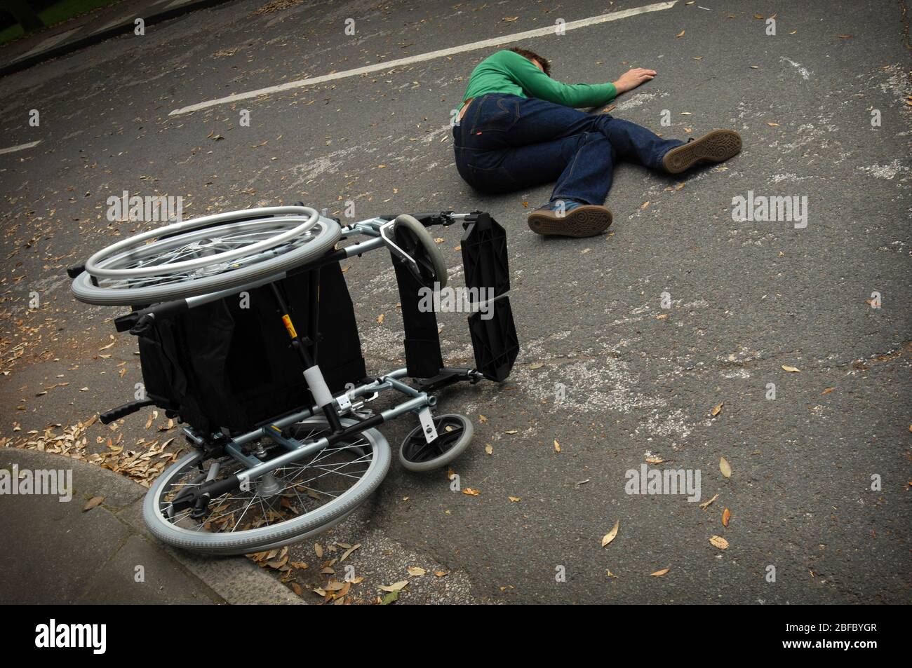 A young man lies on the ground, after falling out of his wheelchair ...