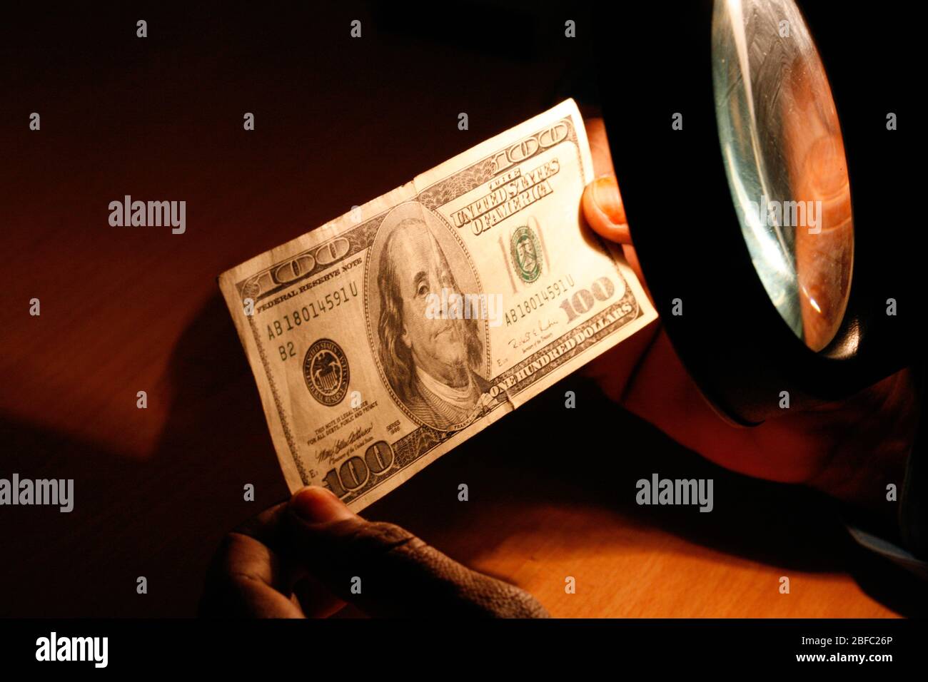 A scientist examines a possible counterfeit one hundred dollar bill ...