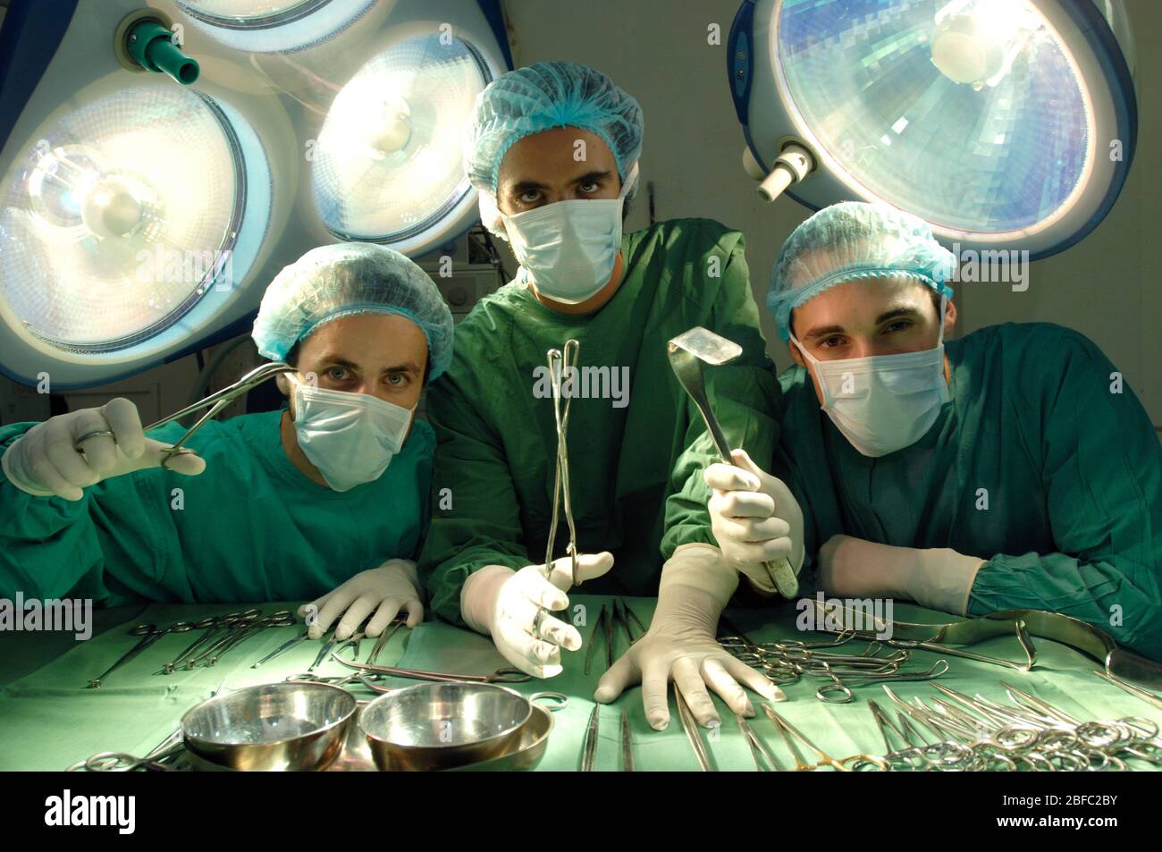 Surgeons stand underneath an operating theatre light; brandishing ...