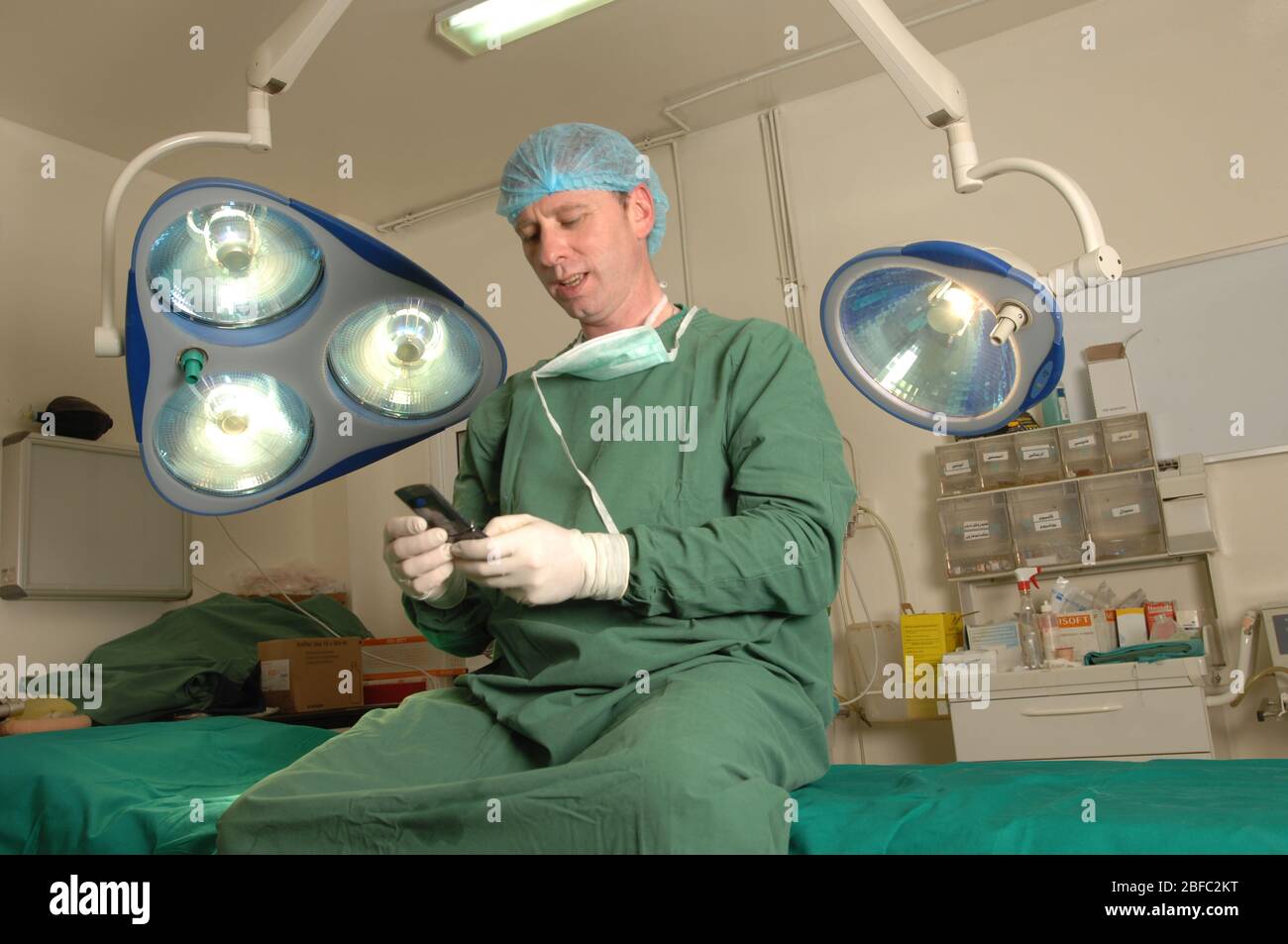 A surgeon sits on the operating table and using his mobile telephone ...