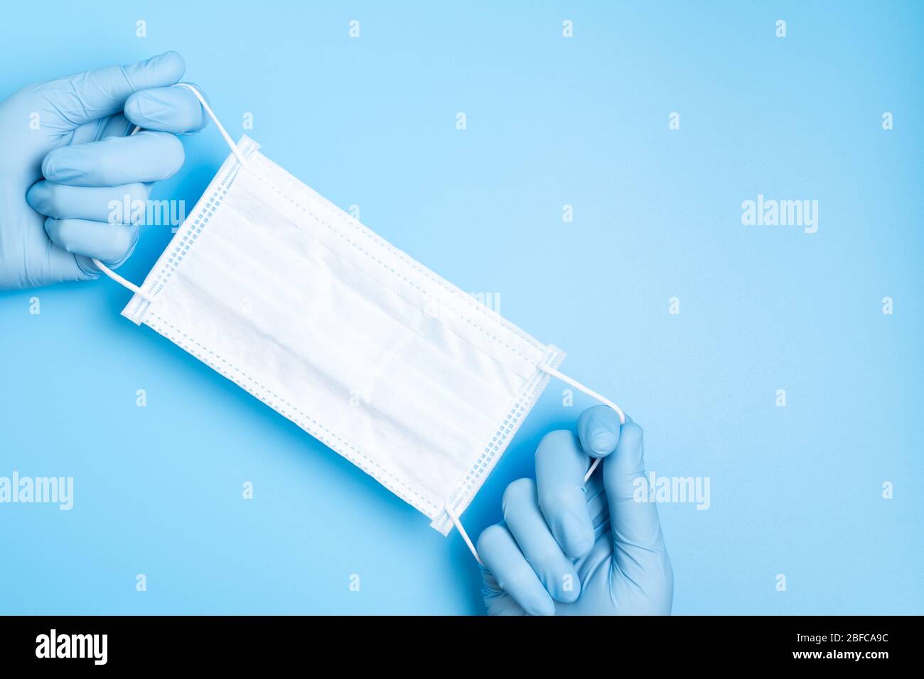 Hand gloves hold face mask in blue background Stock Photo - Alamy