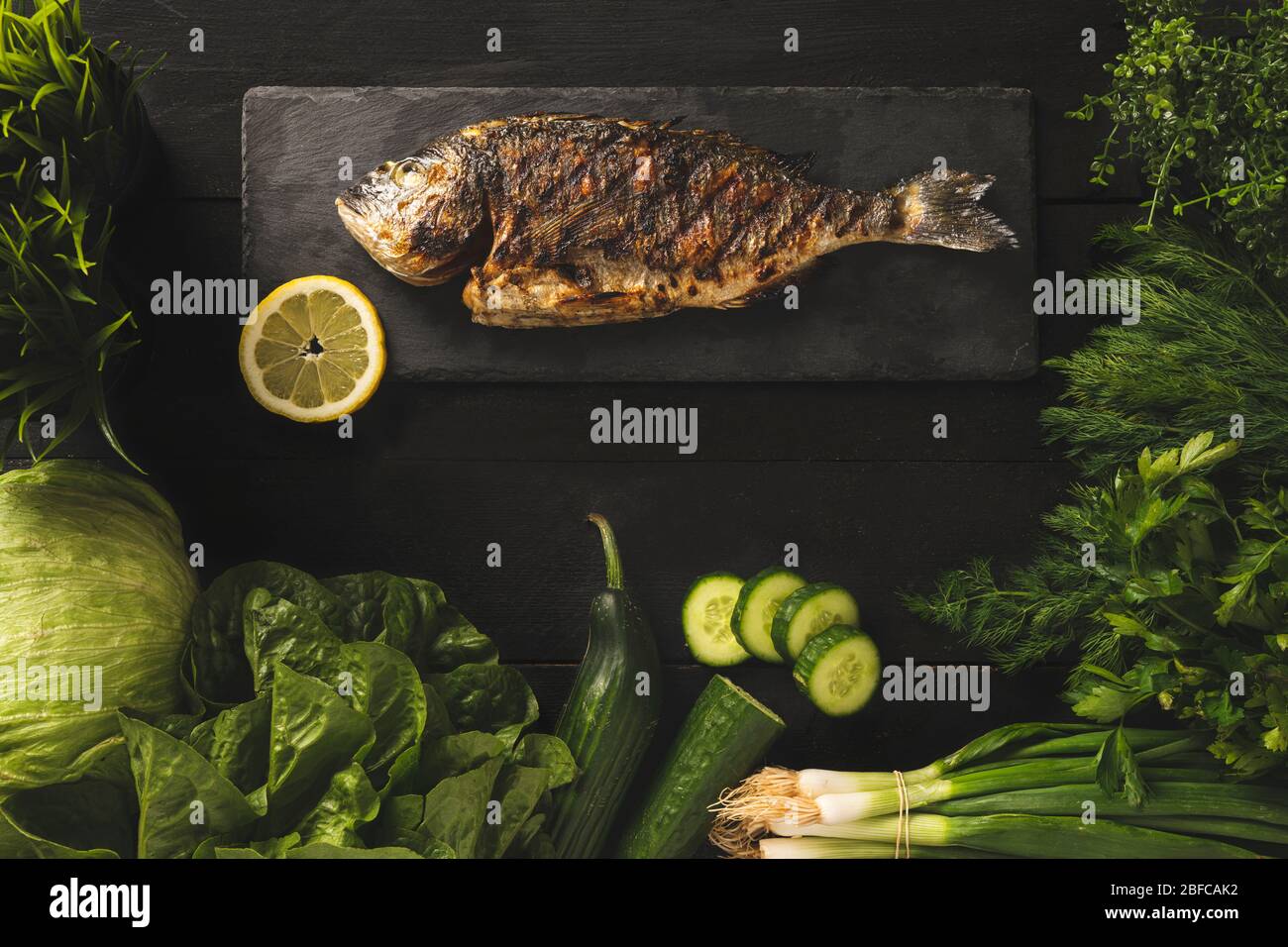 Healthy cooking. Bream fish on a black stone with green vegetables ...
