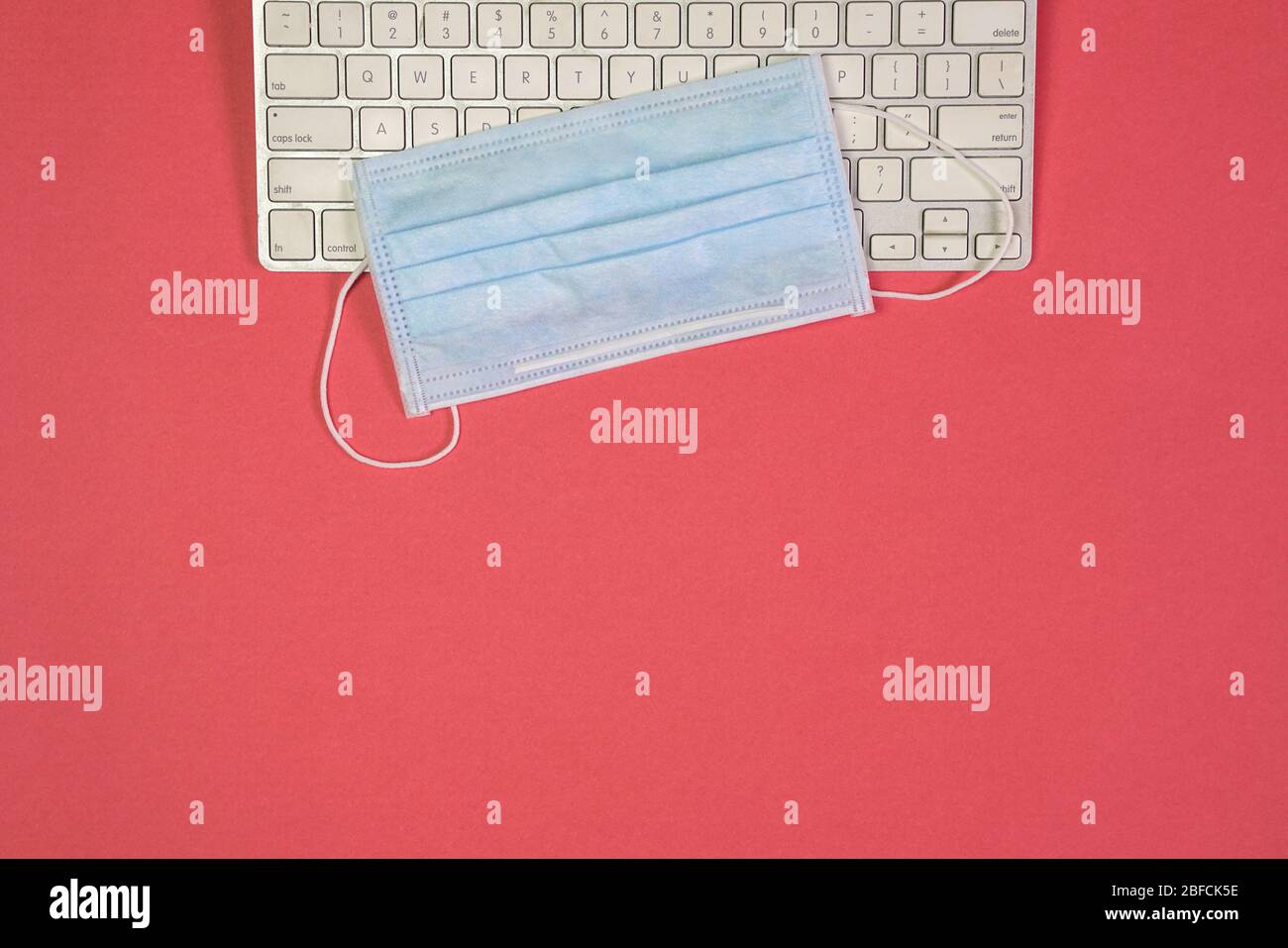 Medical face mask on top of keyboard. Red background. Top view. Copy ...