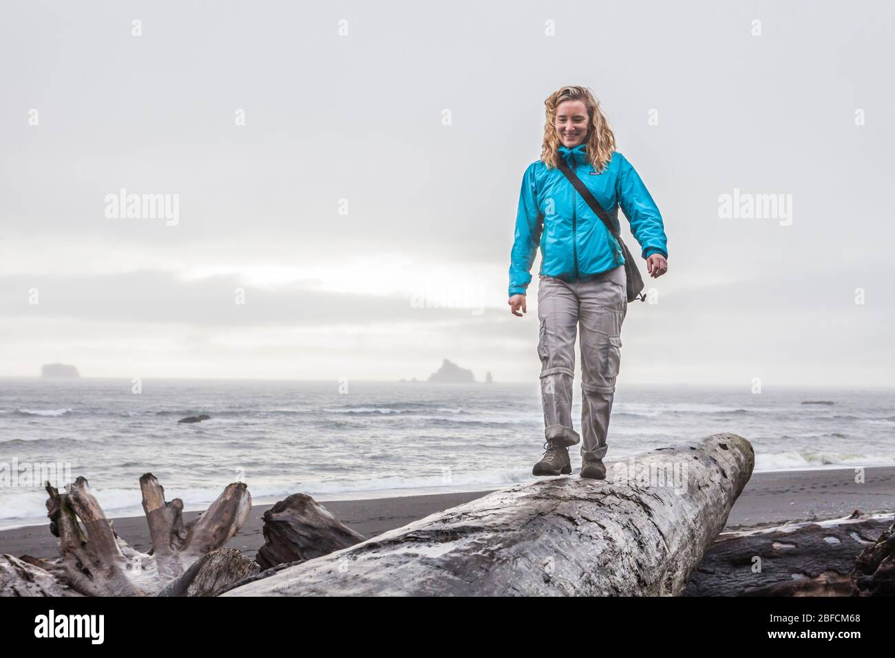 A woman walking on a large driftwood log above a beach. Rialto Beach ...